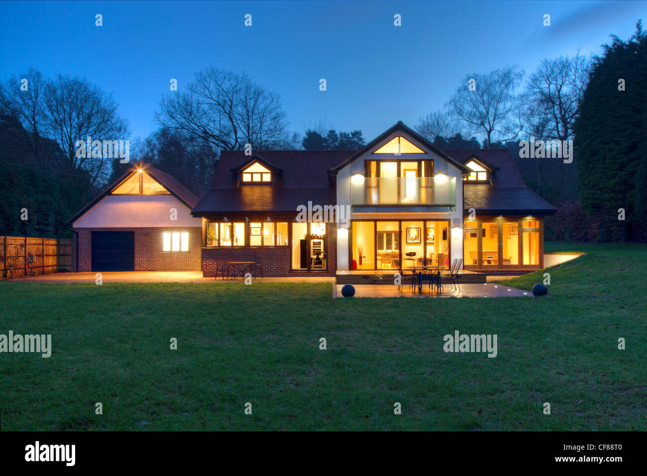 Rear elevation of modern suburban house at dusk fully illuminated, from ...