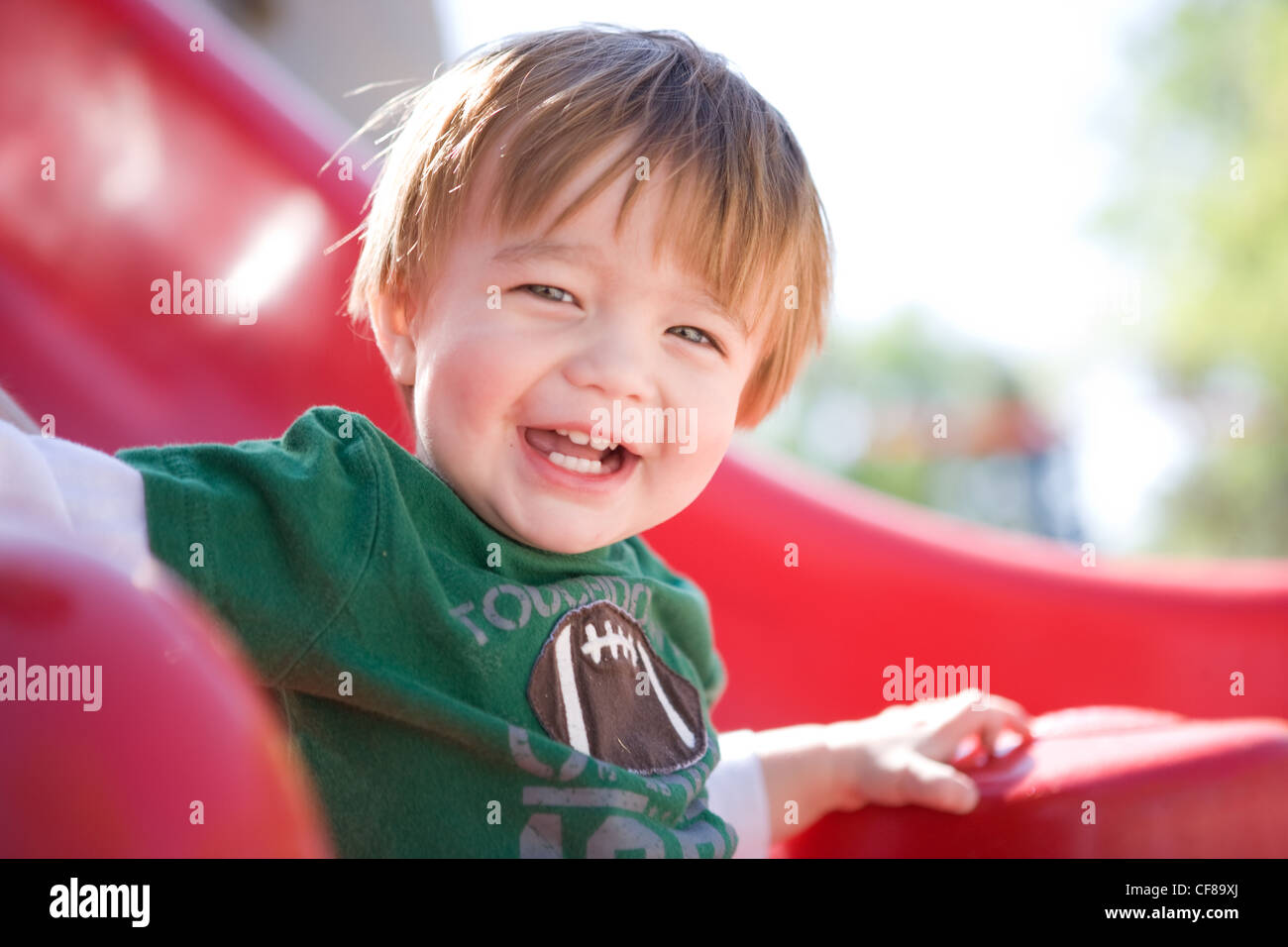 Cute toddler smiling on a red slide at a park Stock Photo - Alamy