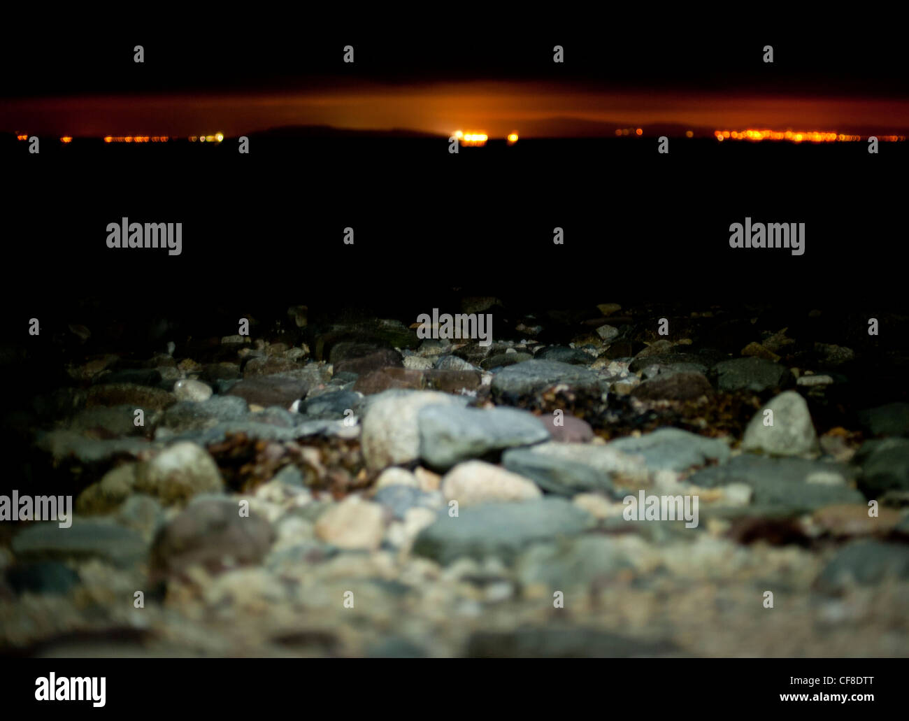 Stones lit up by artificial light on a beach at night with lights from ...