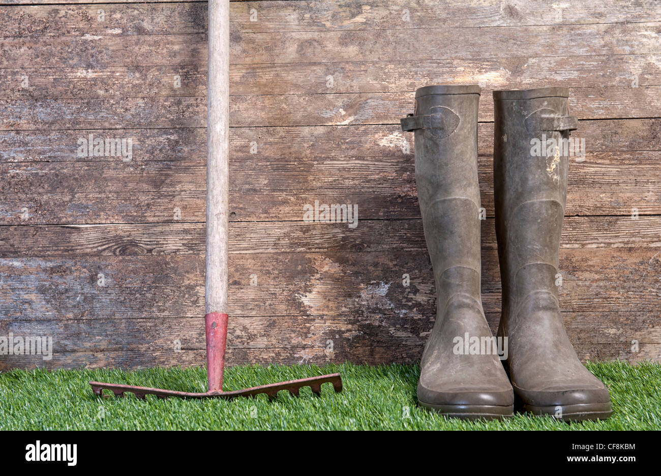 garden boots and rake on grass against an old wooden wall Stock Photo ...