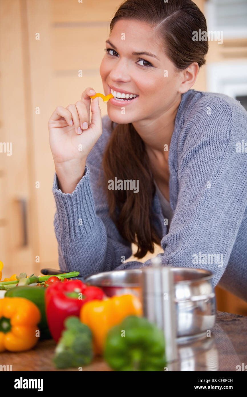 Smiling woman eating a bell pepper in the kitchen Stock Photo - Alamy