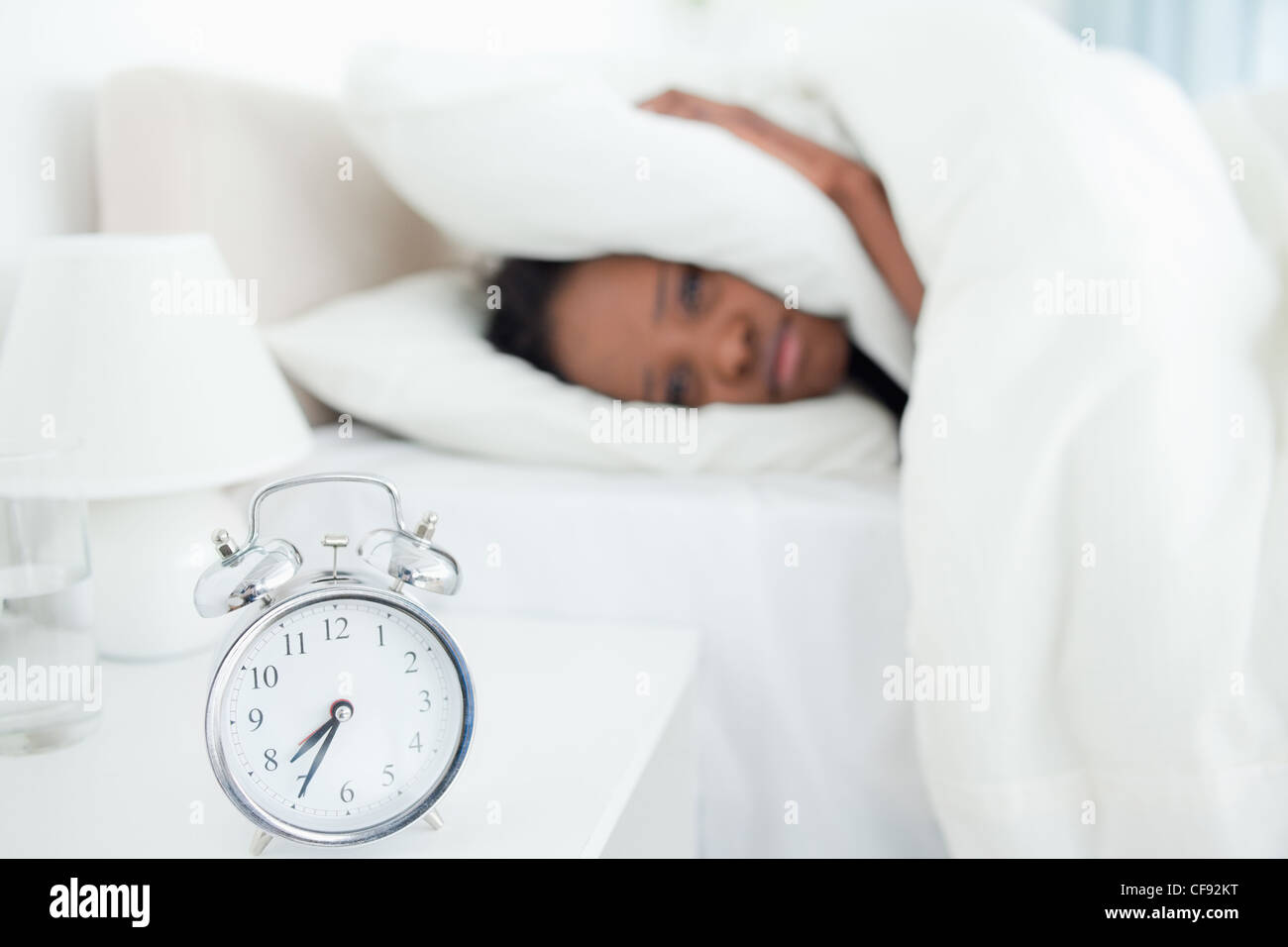 Exhausted woman covering her ears while her alarm clock is ringing ...