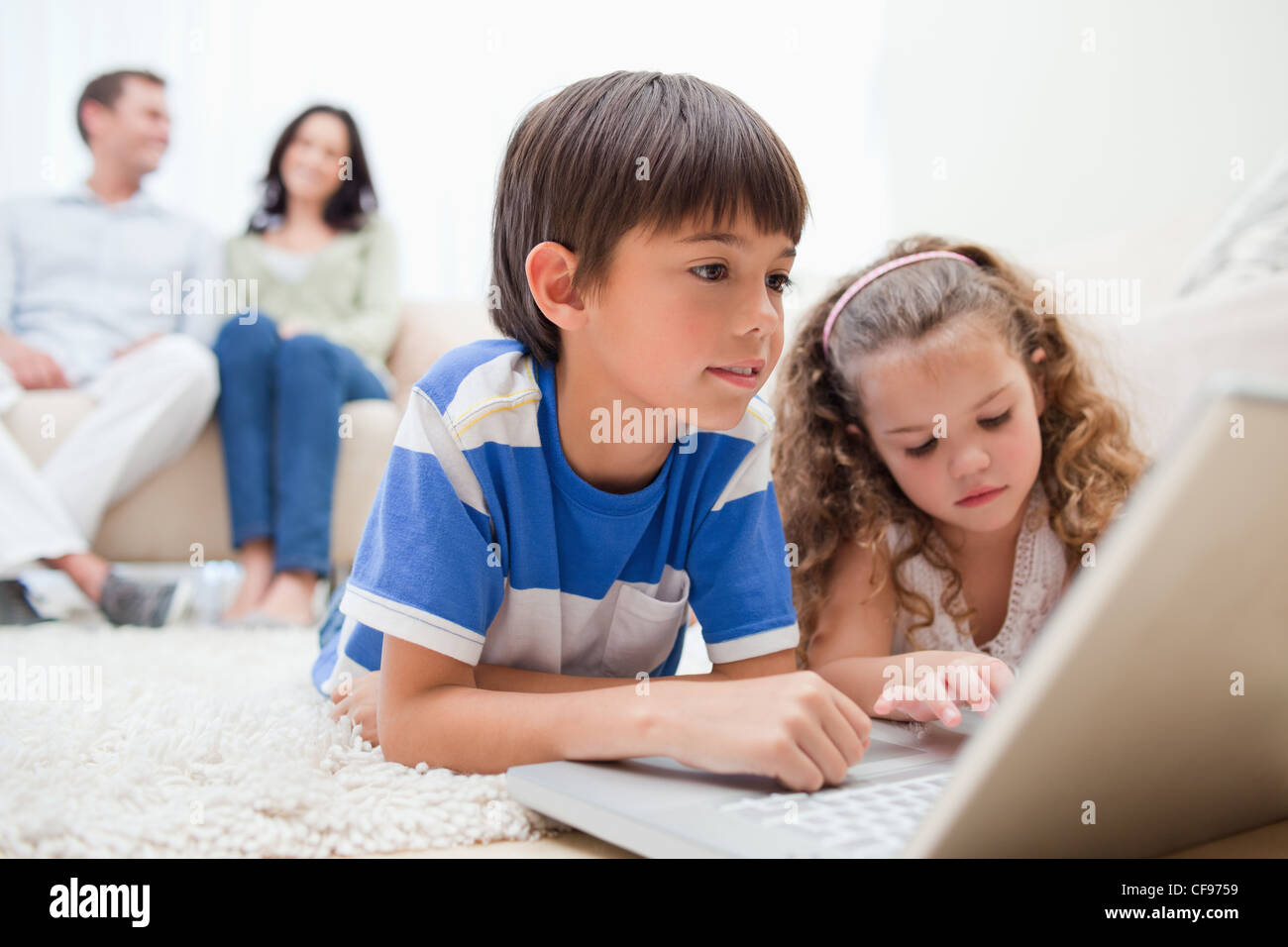 Kids using laptop on the carpet with parents behind them Stock Photo ...