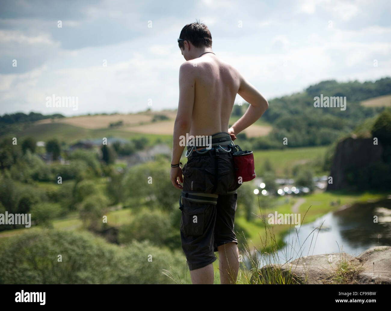 A young male climber in a harness with chalk bag stands at the top of ...
