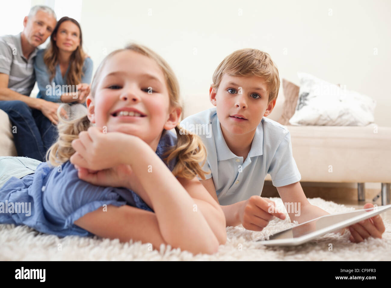 Happy children using a tablet computer with their parents on the ...