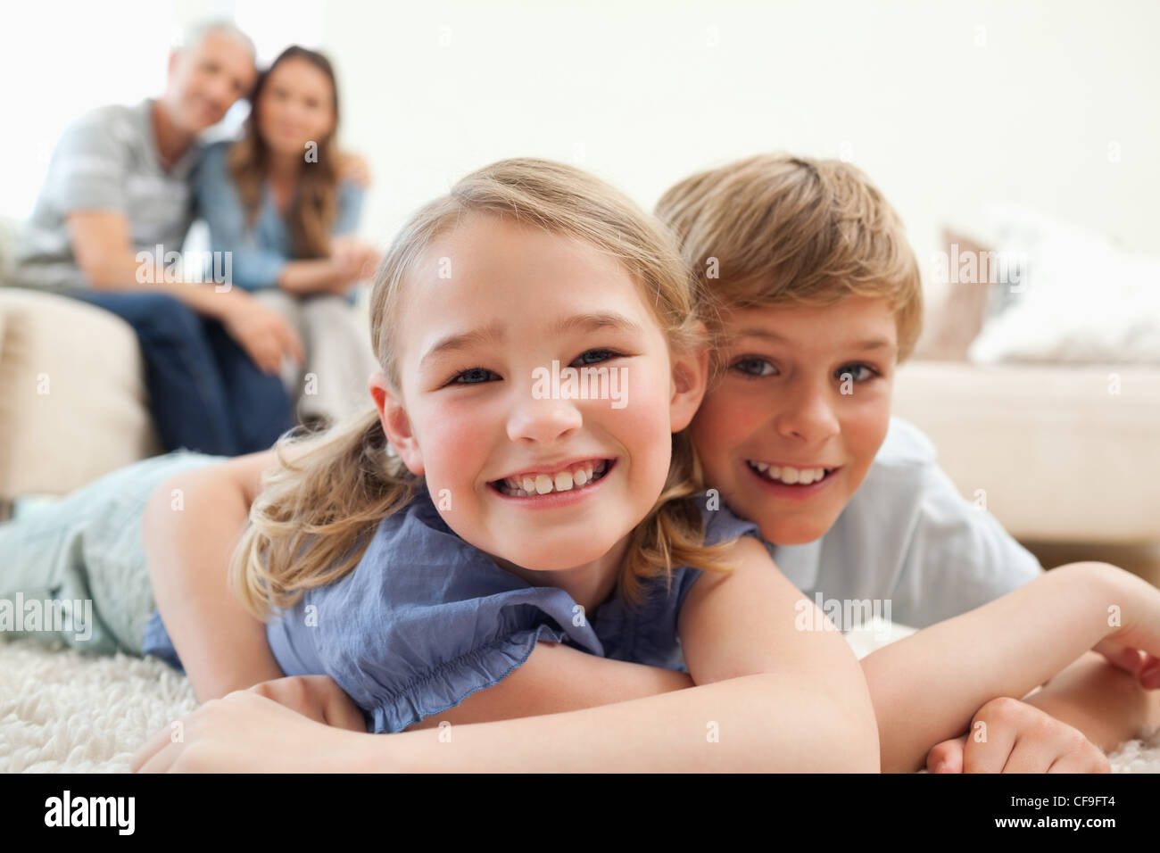 Happy siblings posing on a carpet with their parents on the background ...