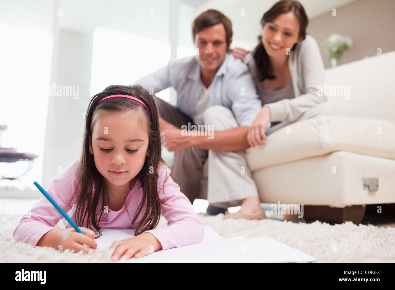 Little girl drawing with her parents in the background Stock Photo - Alamy