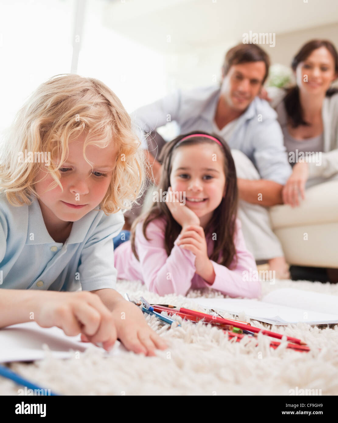 Portrait of siblings drawing while their parents are in the background ...