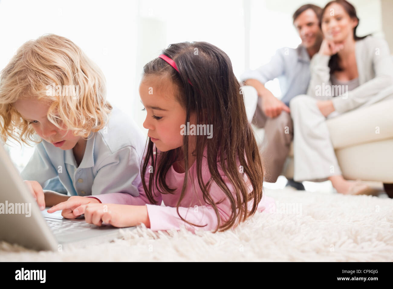 Children using a notebook while their parents are in the background ...
