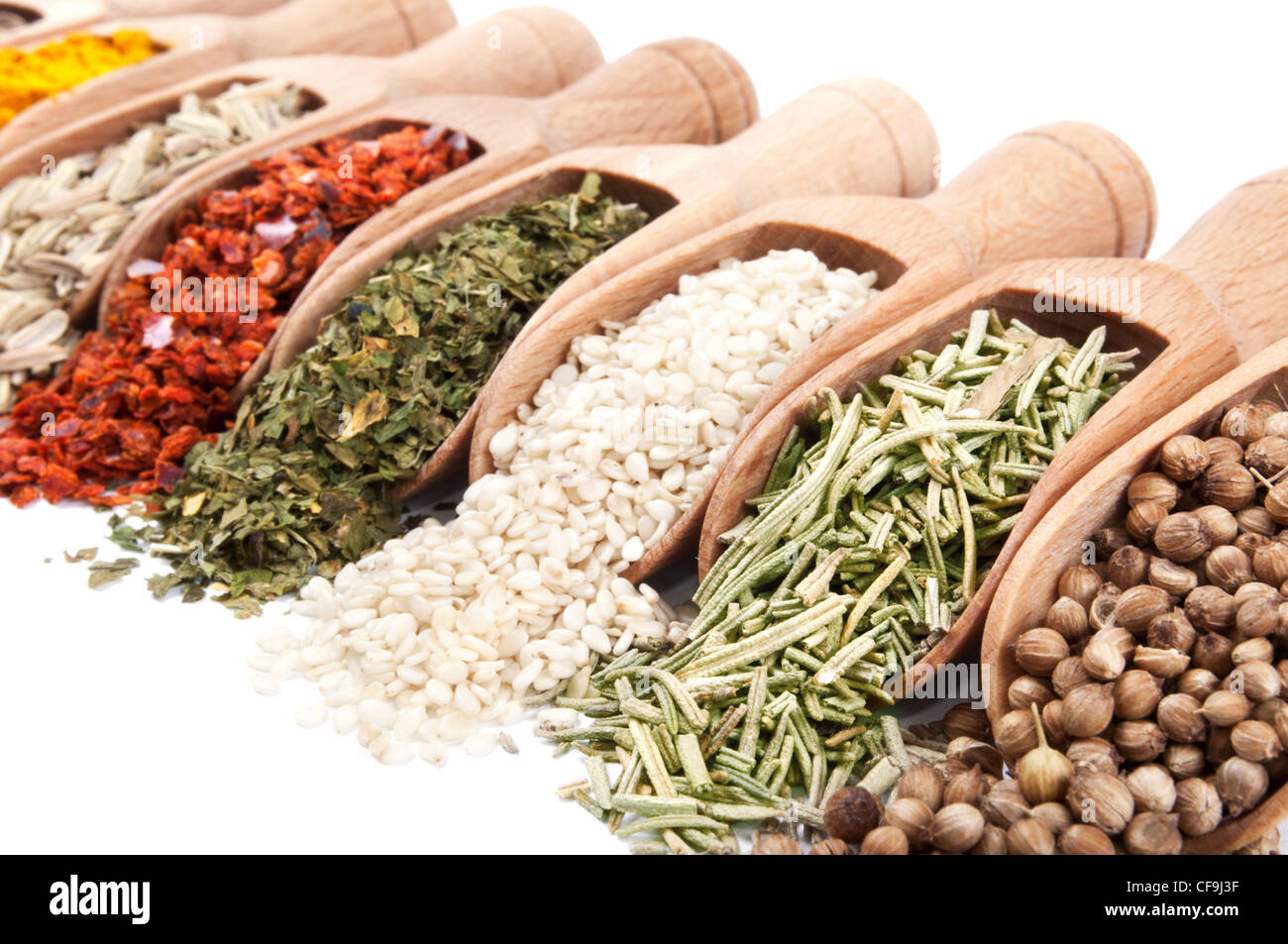 Wooden shovels with different spices scattered from them on white ...