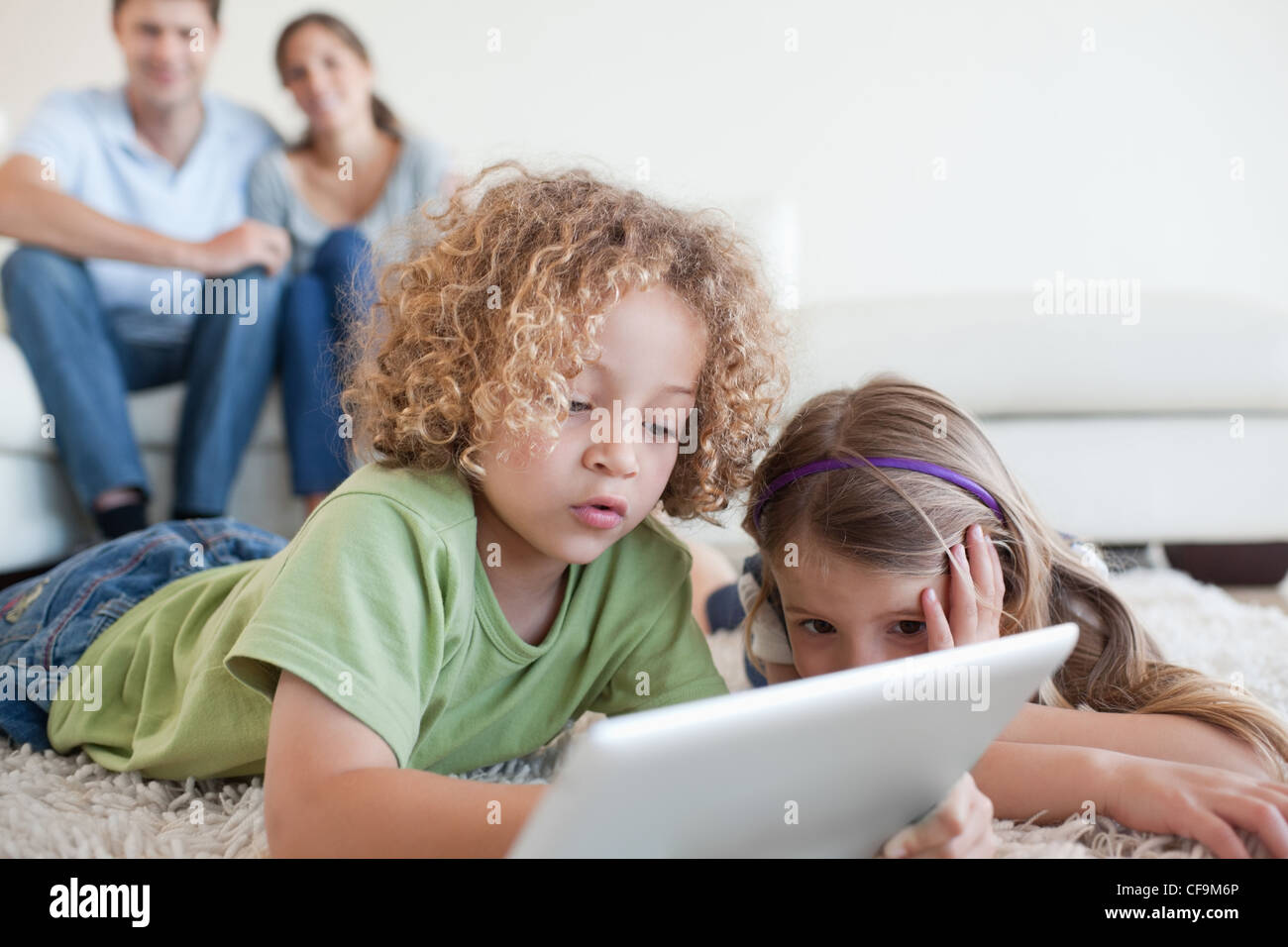 Young children using a tablet computer while their happy parents are ...