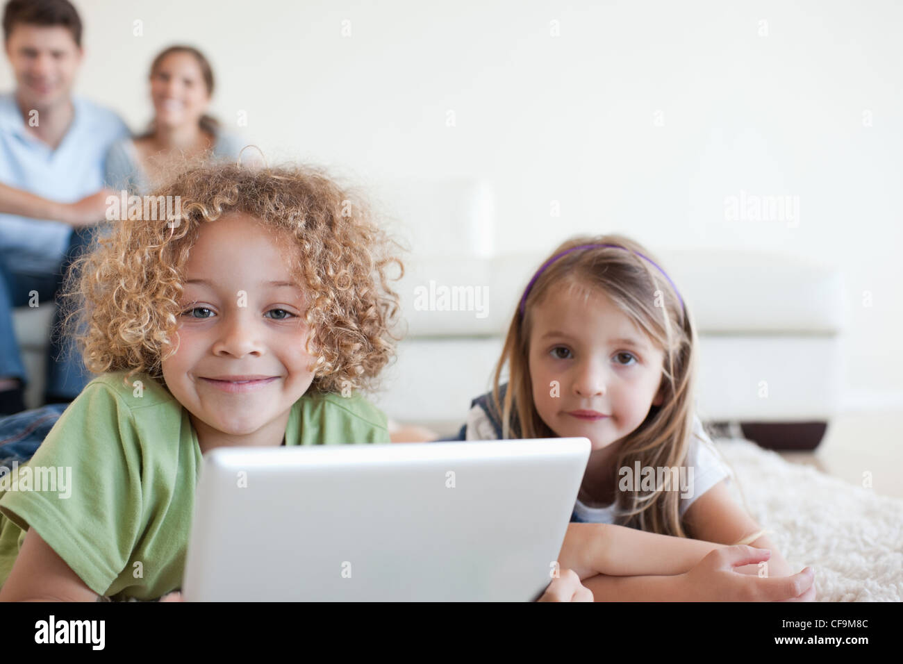 Smiling children using a tablet computer while their happy parents are ...