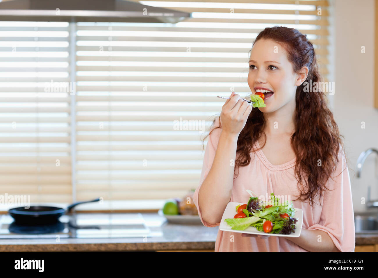 Girl eating some salad in the kitchen Stock Photo - Alamy