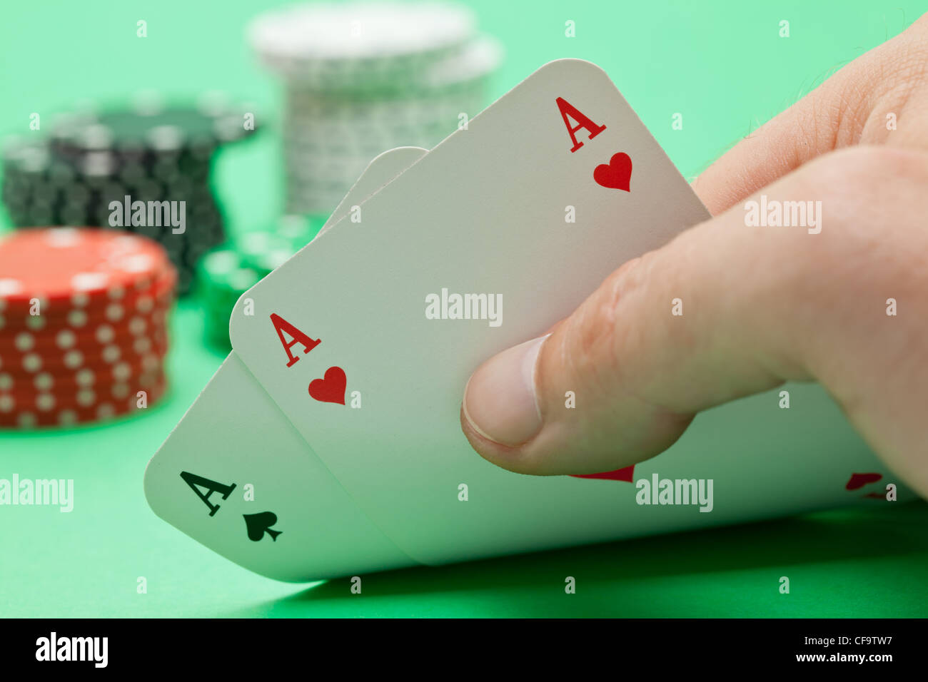 Pokerplayer shows pocket aces with poker chips in the back over green ...