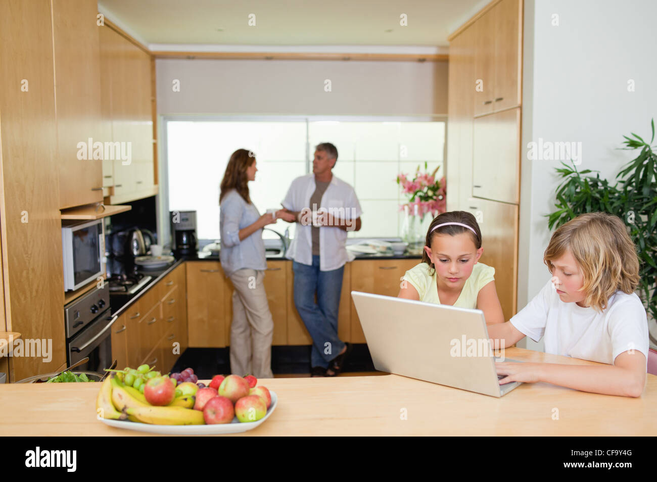 Children with laptop in the kitchen and parents behind them Stock Photo ...