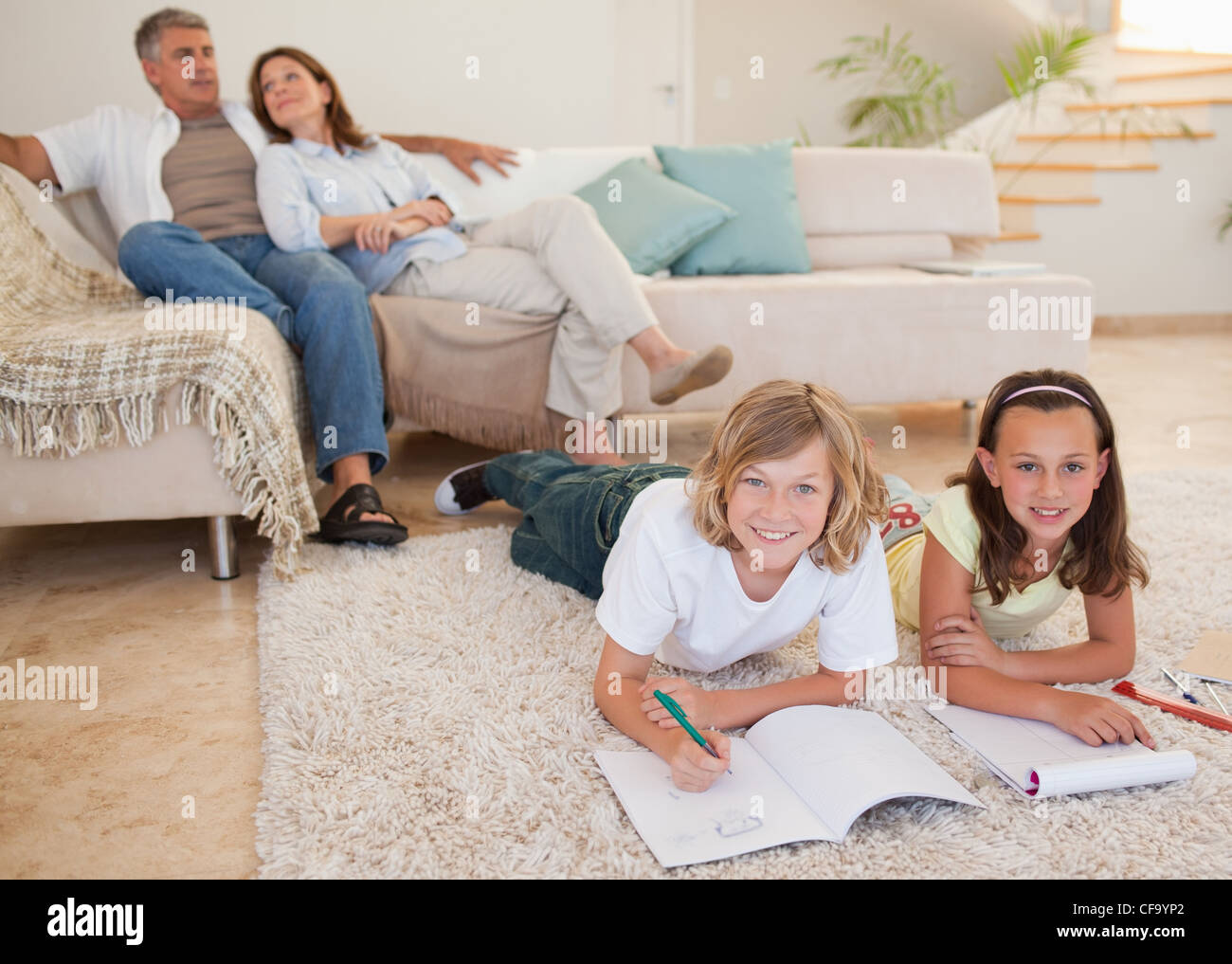 Siblings doing homework on the carpet with parents behind them Stock ...