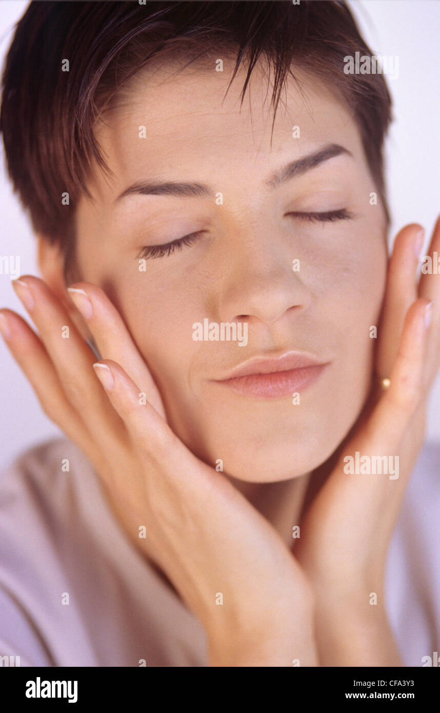 Brunette female with short hair, eyes shut and hands cupped over cheeks ...