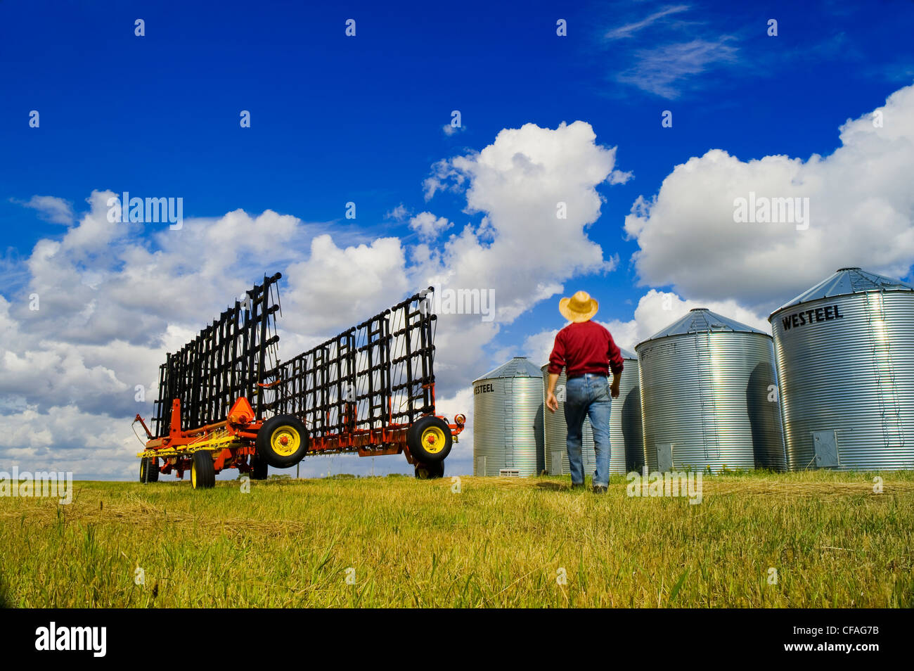 a man lwalks towards harrowing equipment next to grain storage bins ...