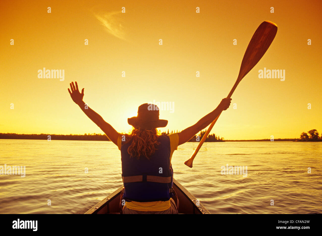 Female canoeist, arms raised welcoming the sunset, Otter Falls ...