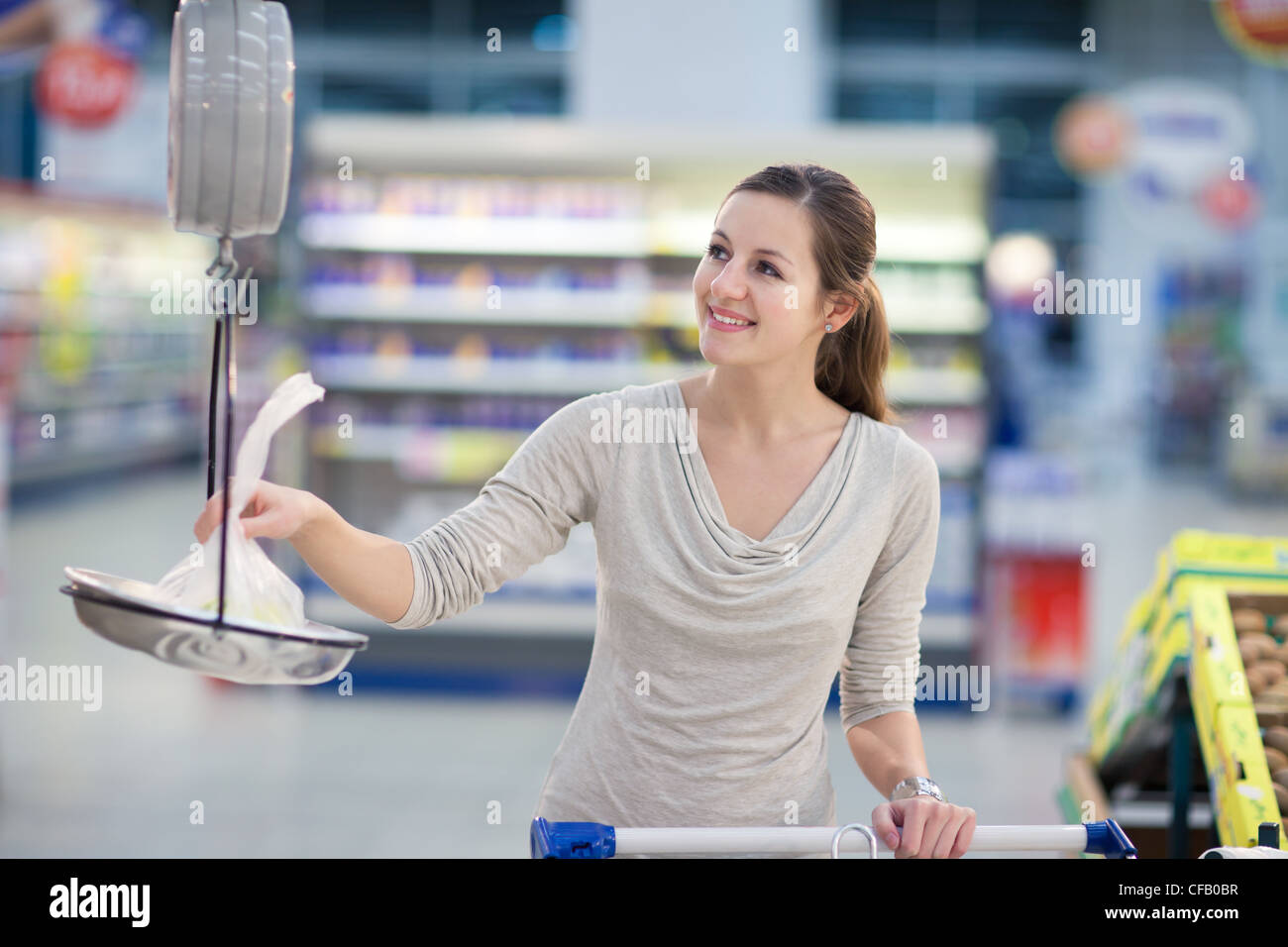 Young woman using a weighing scale while shopping for fruit and ...