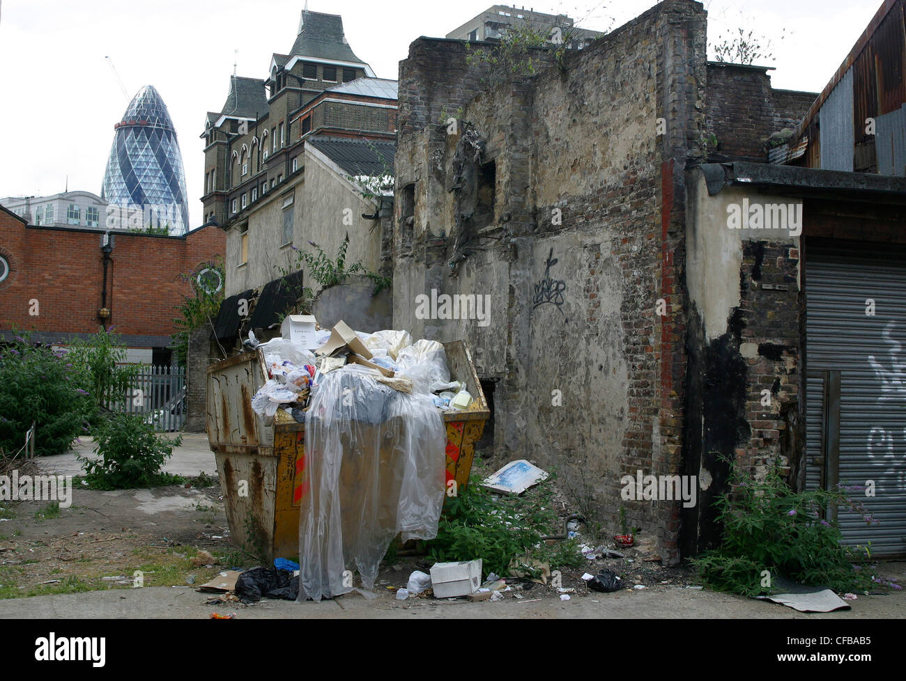 An overflowing skip standing next to a crumbling wall, with the gherkin ...