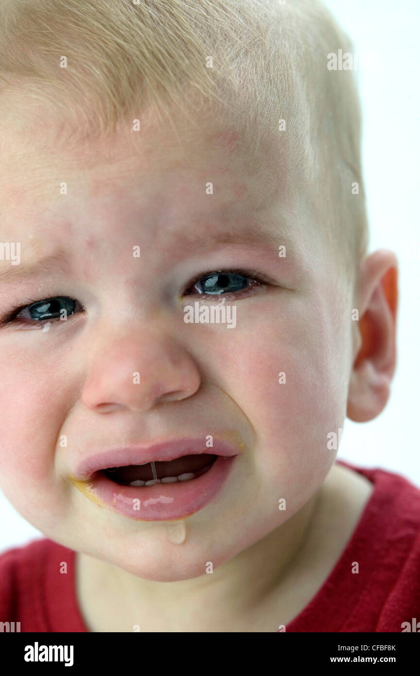 Male baby wearing red top, crying looking to camera with mouth open ...