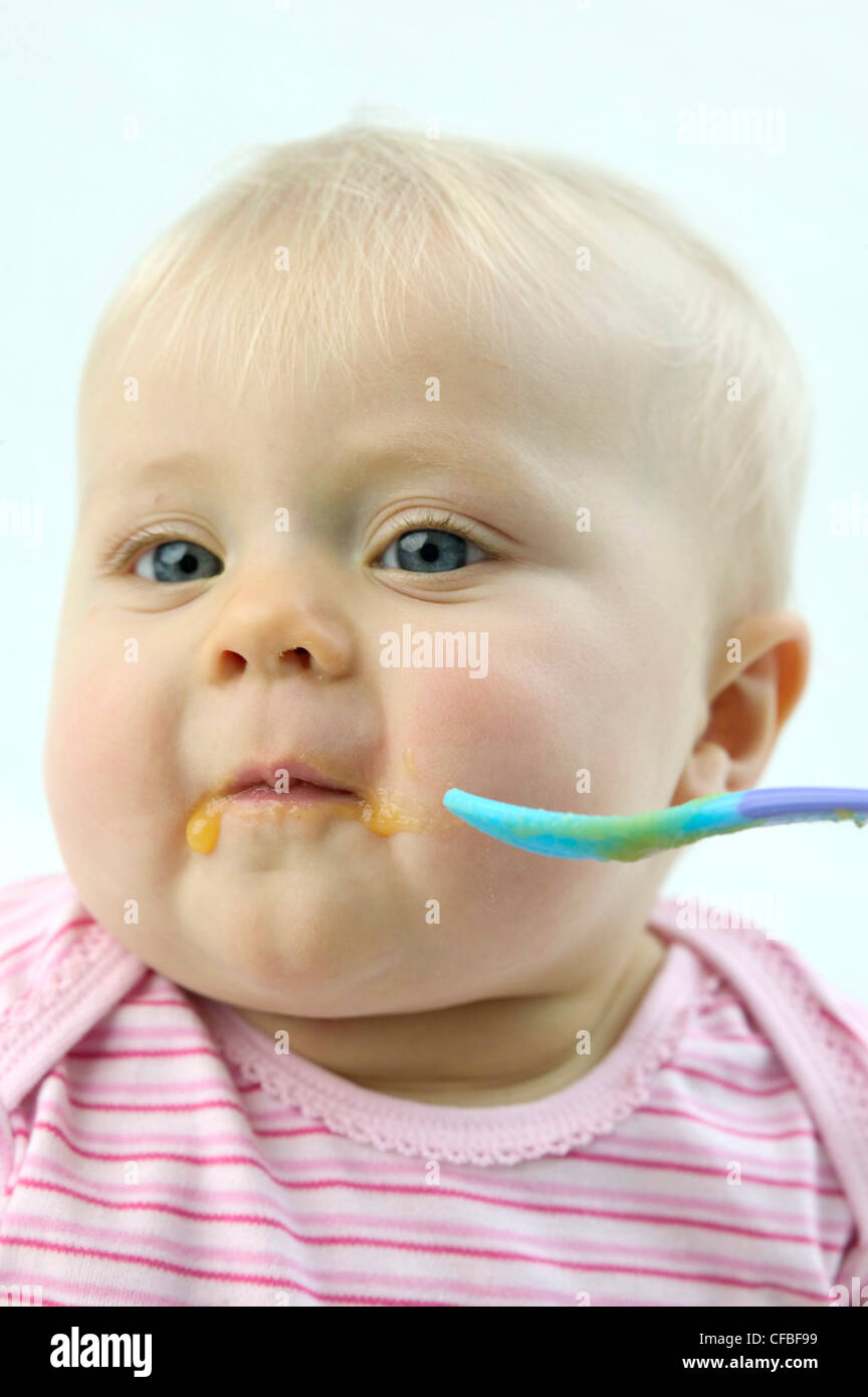 Female baby wearing pink striped babygro, being fed from plastic spoon ...