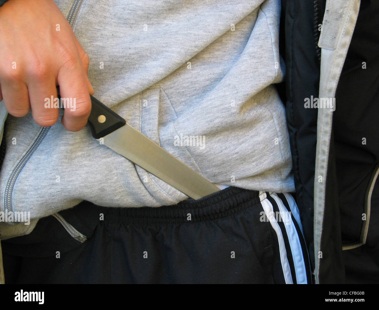 Close up of teenage male pulling knife out of waistband of tracksuit ...