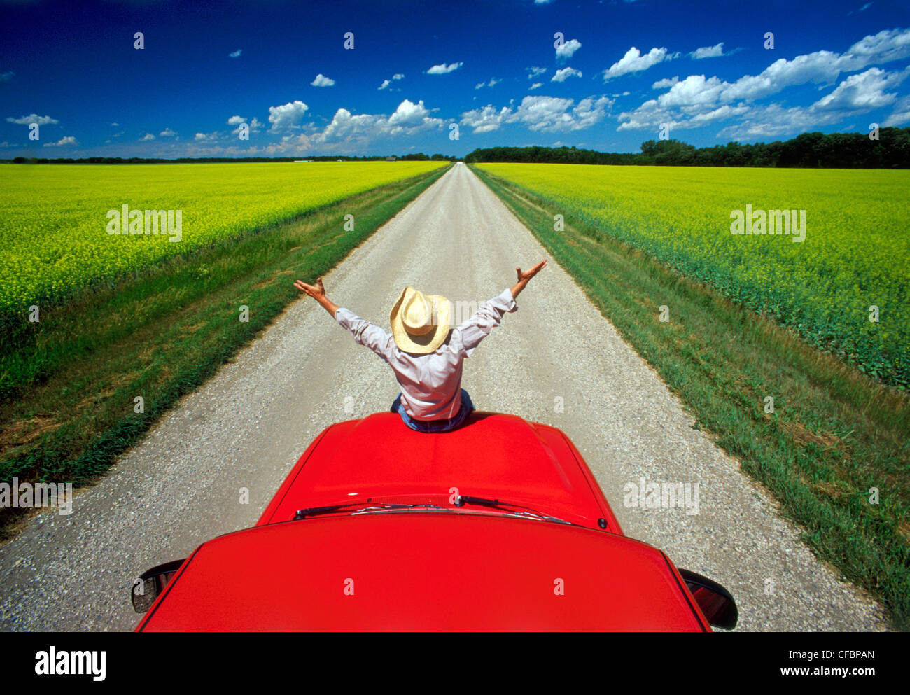A man sits on the front of his truck overlooking a country road with ...