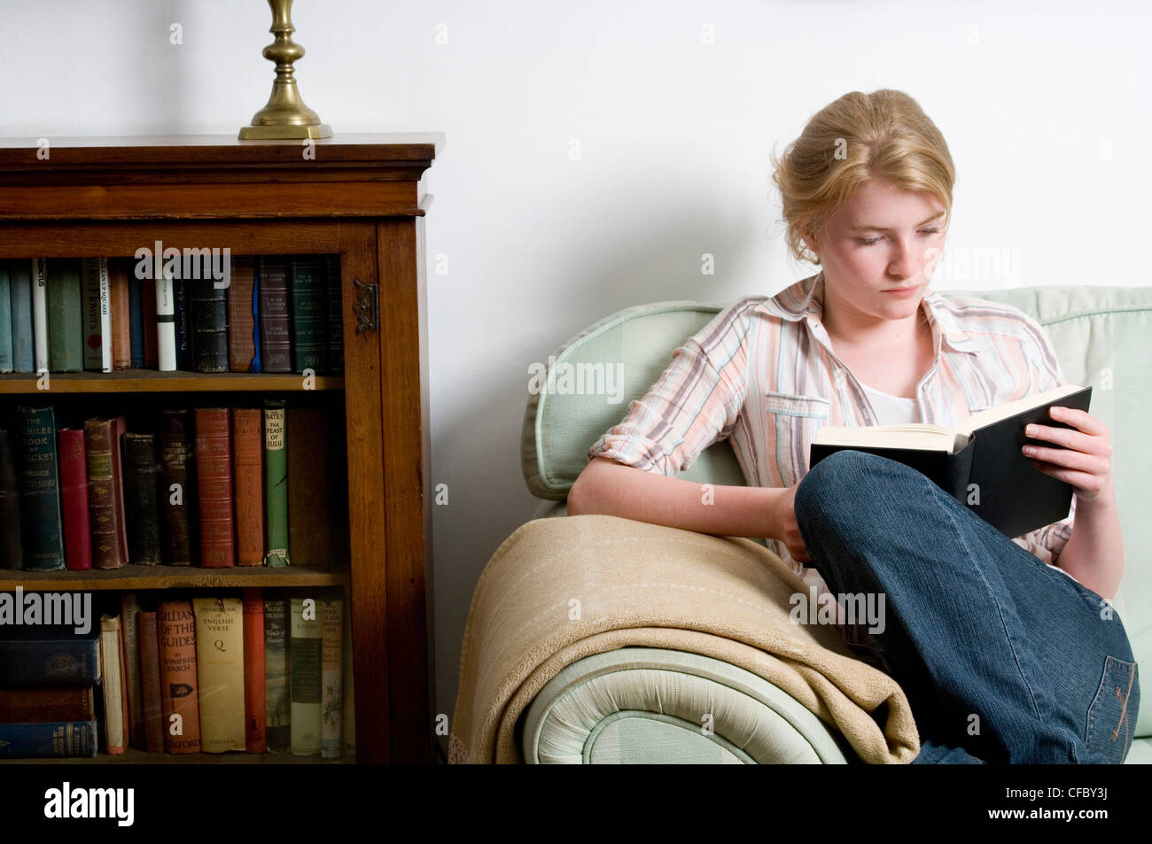 Female sitting on a sofa reading a book Stock Photo - Alamy
