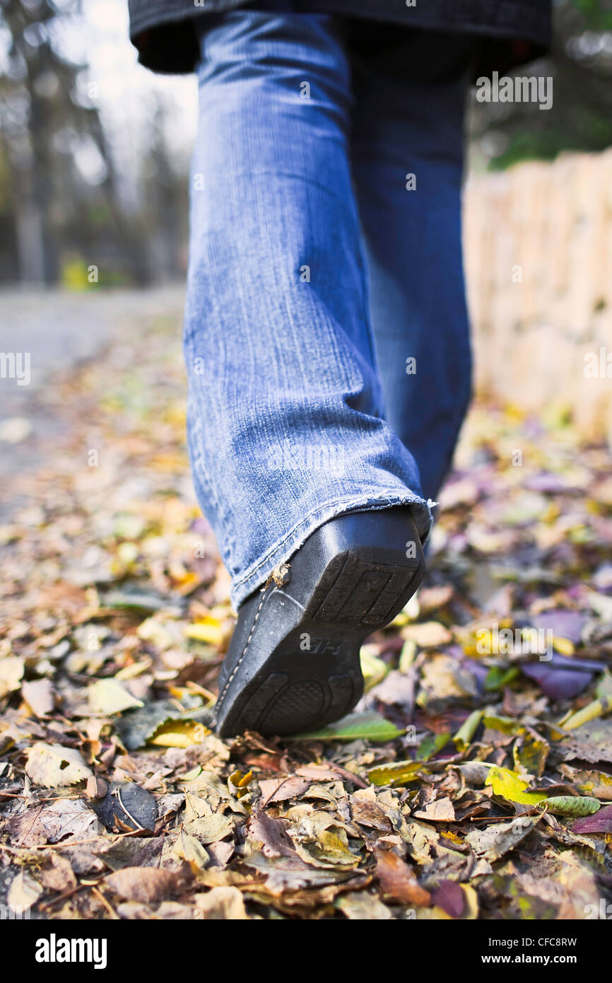 Rear low angle view of a woman walking down a leaf covered path in ...