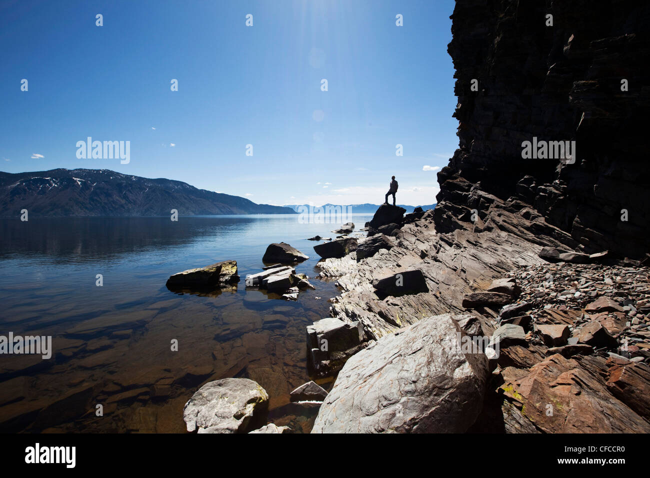 A male figure stands on a rock at the edge of a beautiful lake on a ...