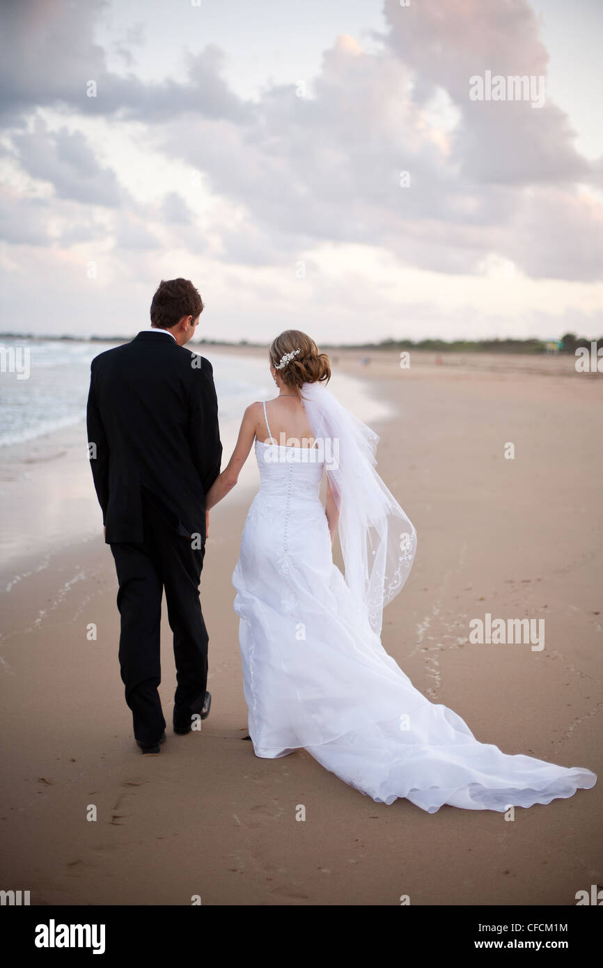 Bride and Groom holding hands and walking on a beach, with backs to ...
