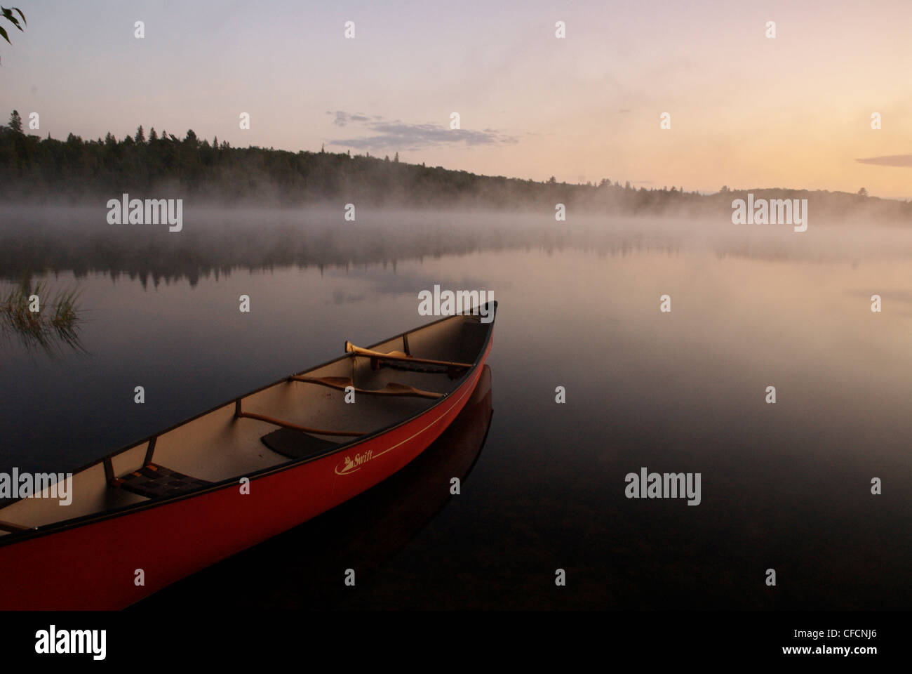 Canoe on shore with predawn scene of a wilderness lake in background in ...