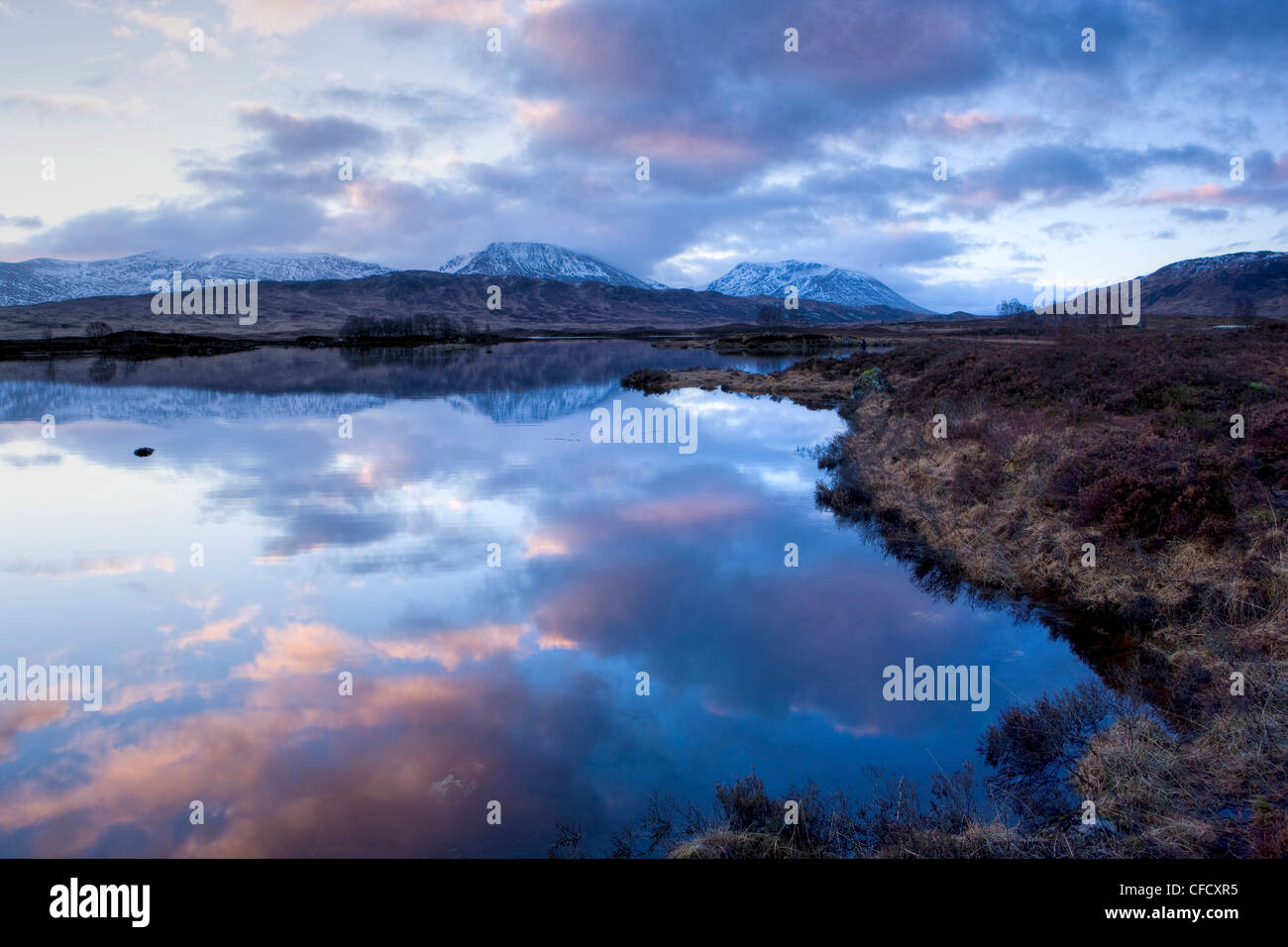 Dawn view of Loch Ba reflecting the sky and distant snow-capped ...