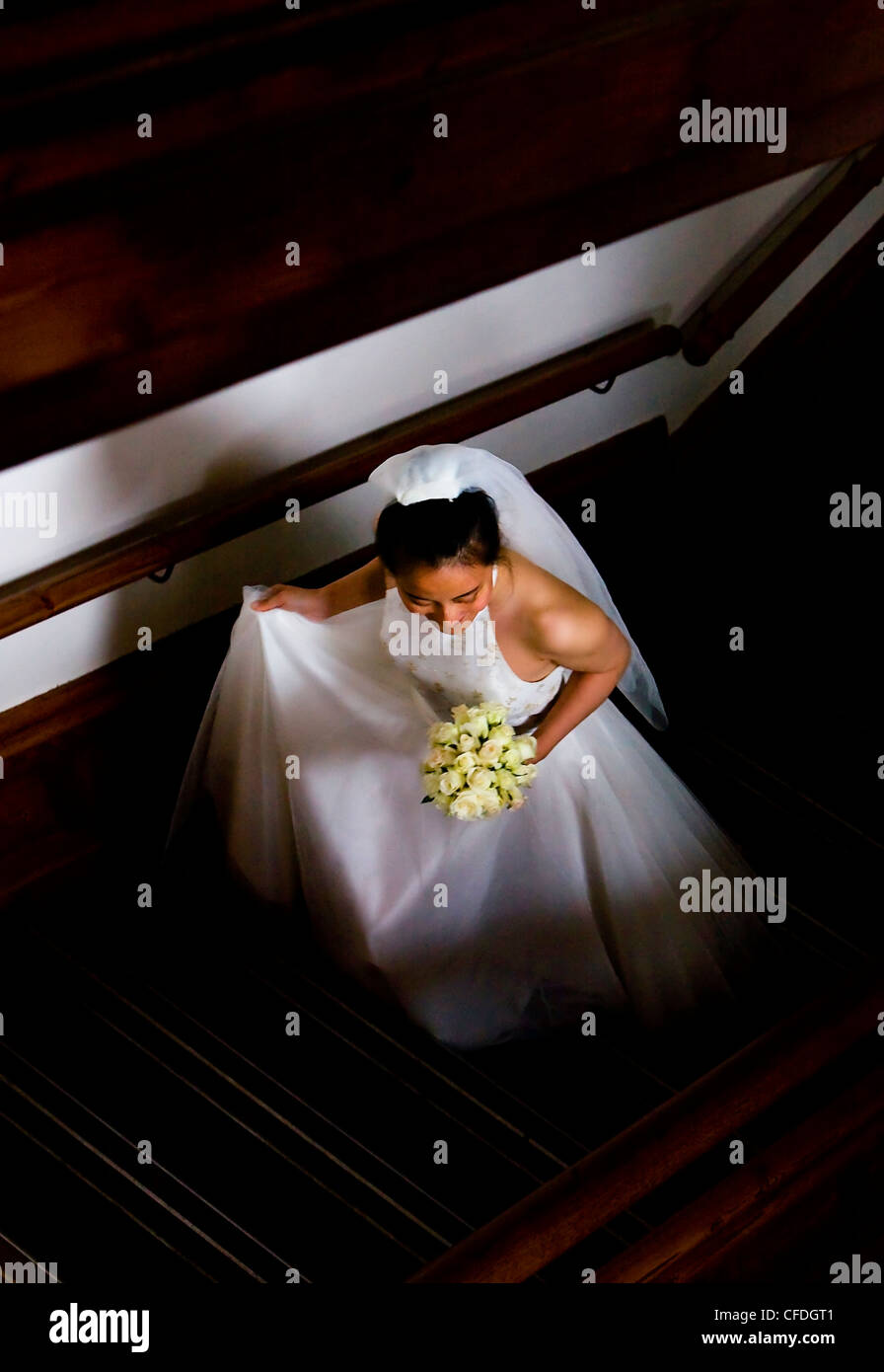 Bride is walking up the wooden staircase holding her wedding dress and ...