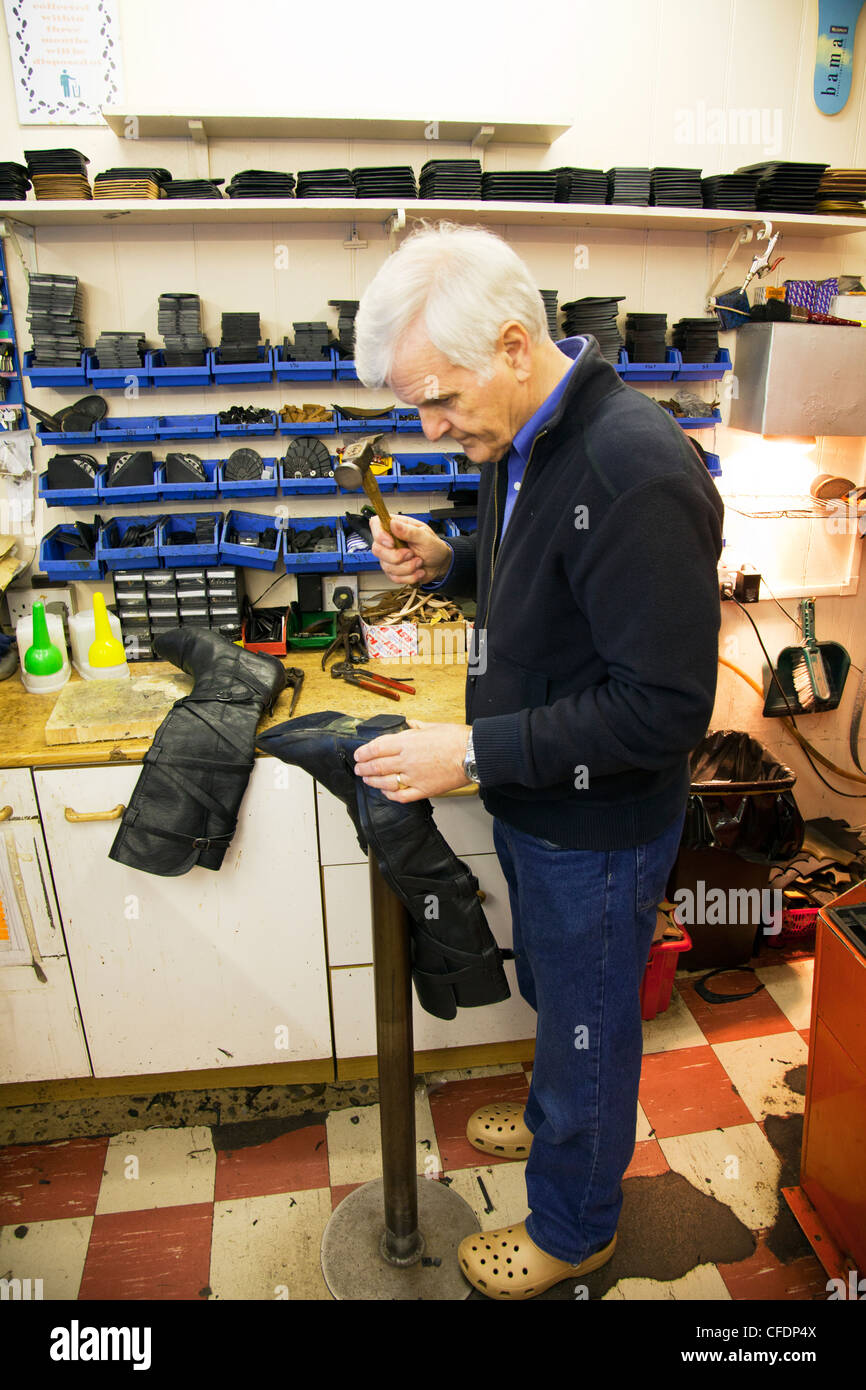 Shoe repairer mending shoes in cobblers shop working on last to hammer ...