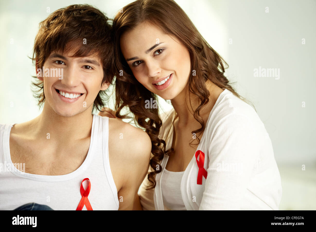 Smiling guy and girl with red ribbon badges sitting together and ...