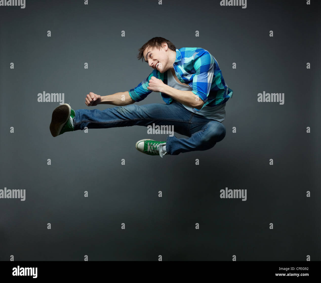 Energetic guy jumping with fists clenched tight and kicking the air ...