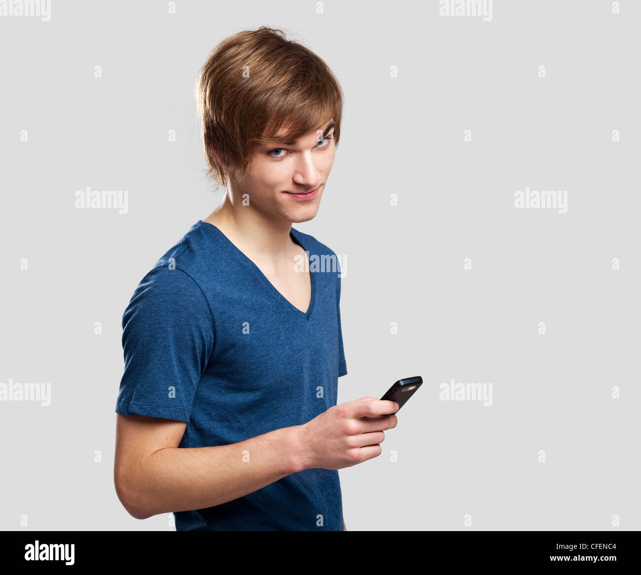 Portrait of handsome young man sending text messages with is mobile phone, over a gray ...