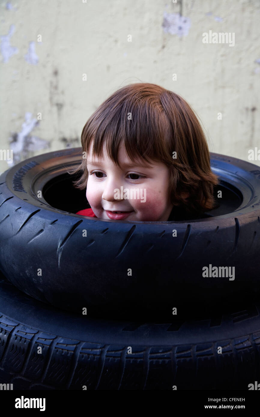Three year old boy playing in stack of tyres Stock Photo - Alamy