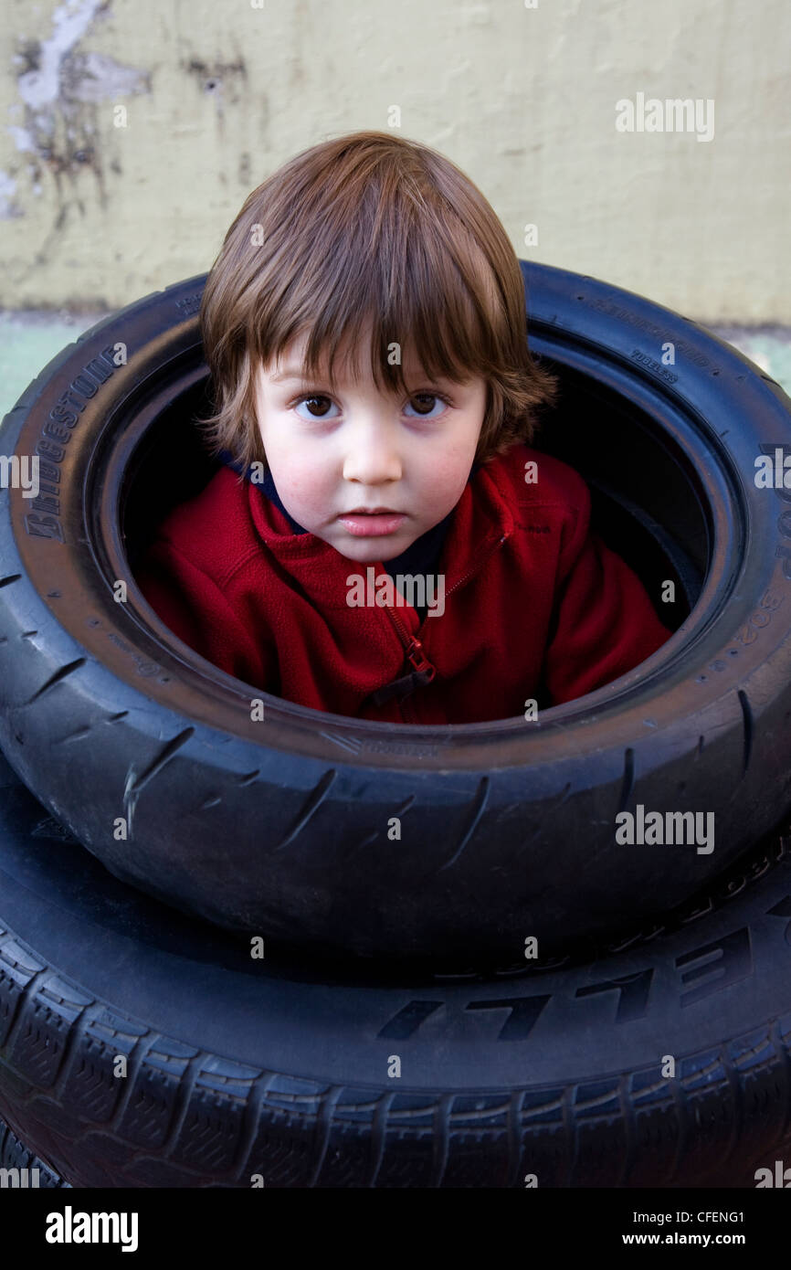 Three year old boy playing in stack of tyres Stock Photo - Alamy