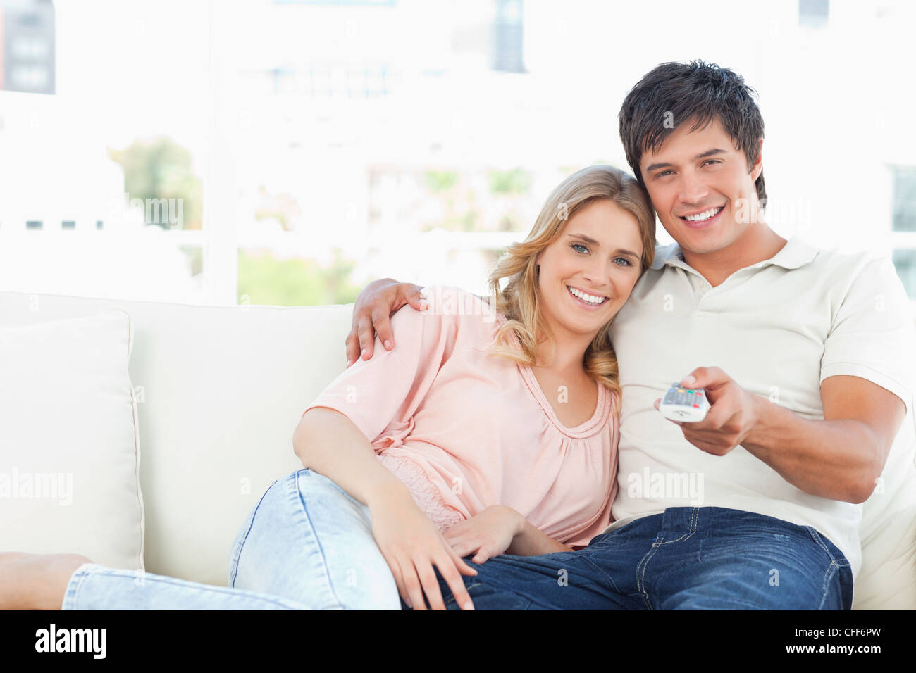 Man and woman on the couch together, turning the channel on the tv ...
