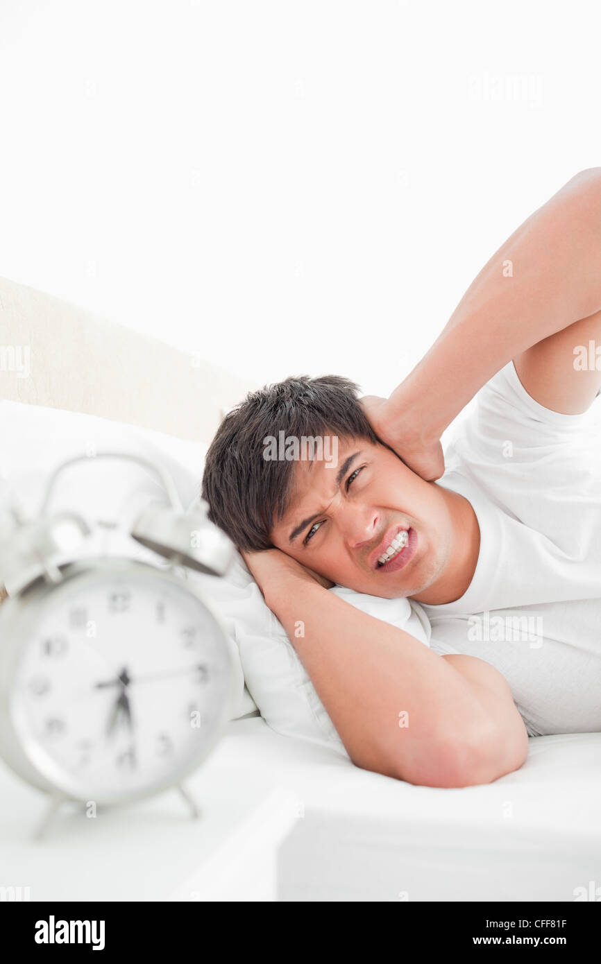 Man covering his ears in anger as the alarm clock rings loudly Stock ...