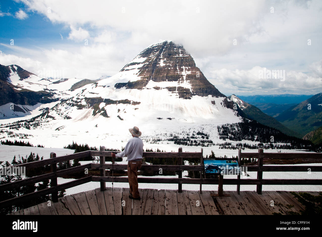 An older man stands at an overlook as peaks with snow rise in the ...
