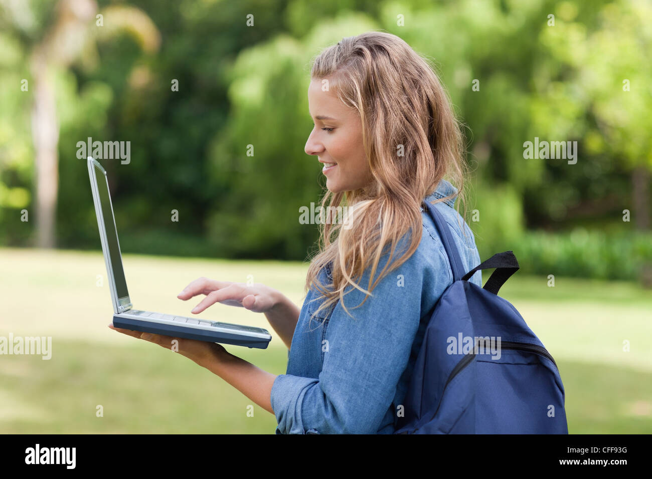 Side view of a teenage girl holding her laptop while standing in a park ...