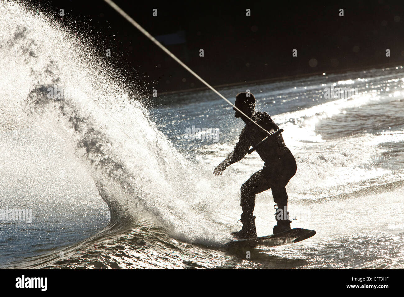 A professional wakeboarder carves and slashes on a lake at sunset in ...