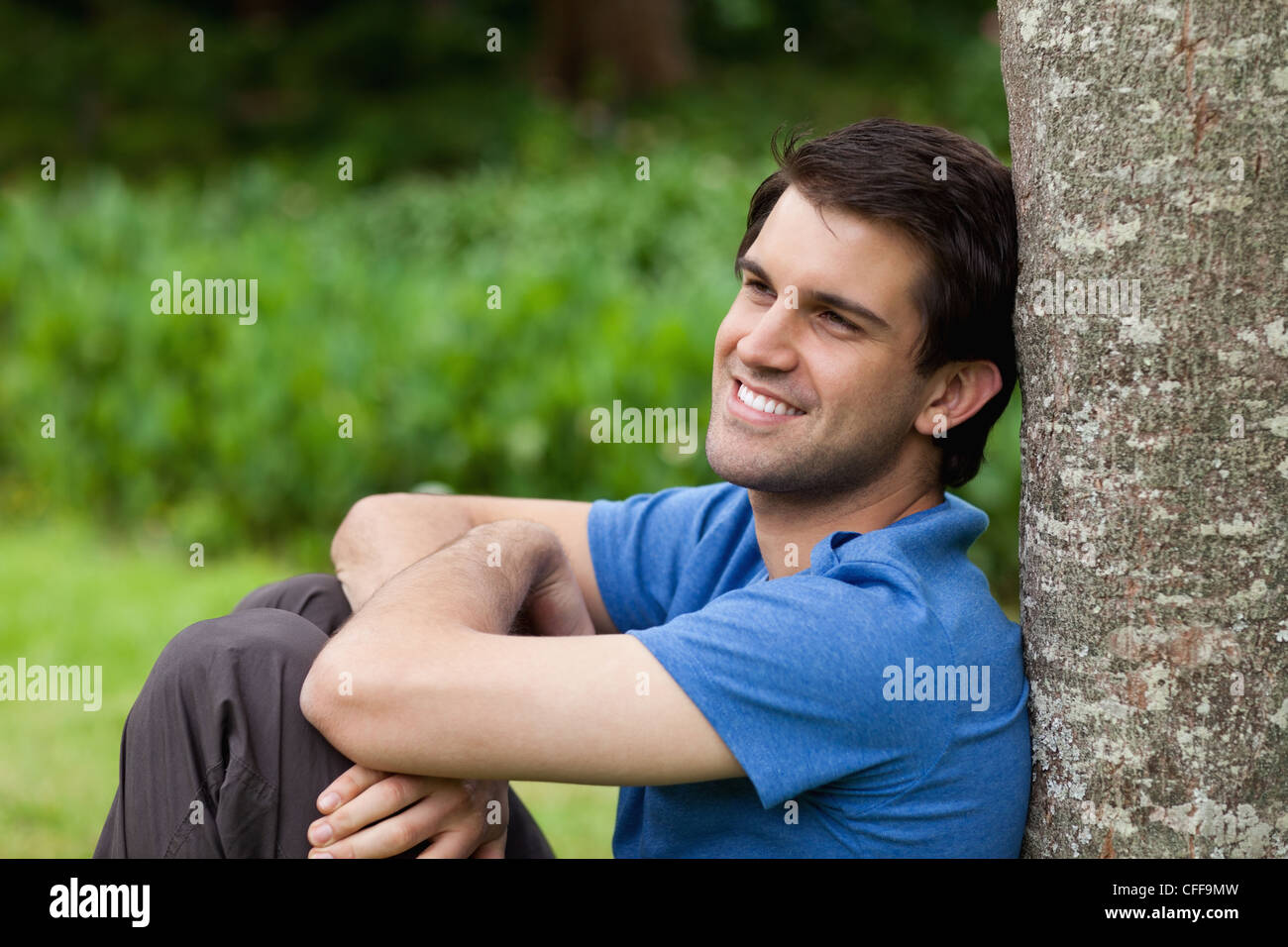 Young man leaning against a tree while crossing his arms Stock Photo ...