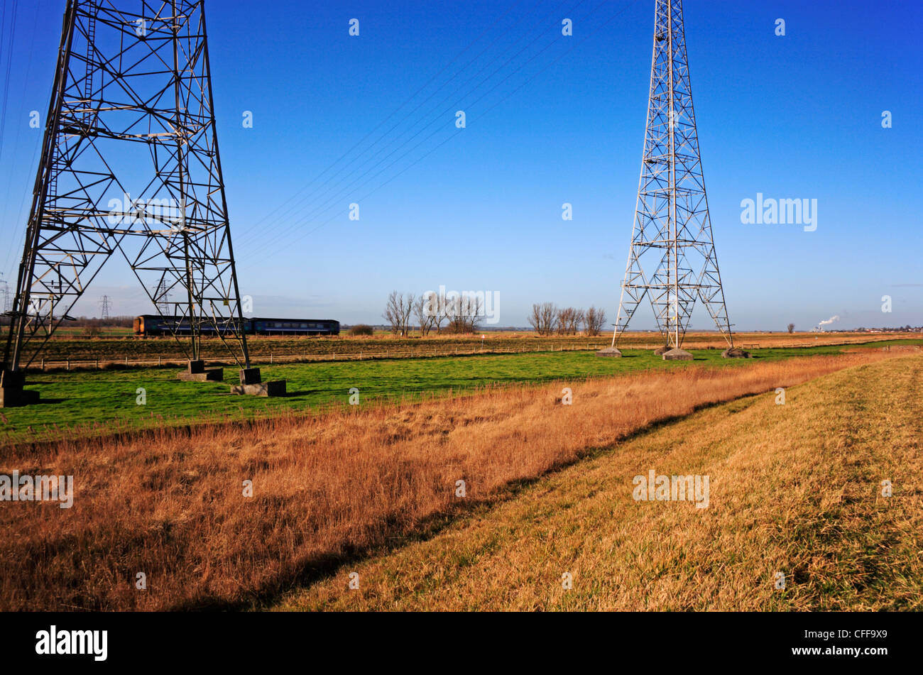 A view of power line pylons and railway with train crossing marshes ...