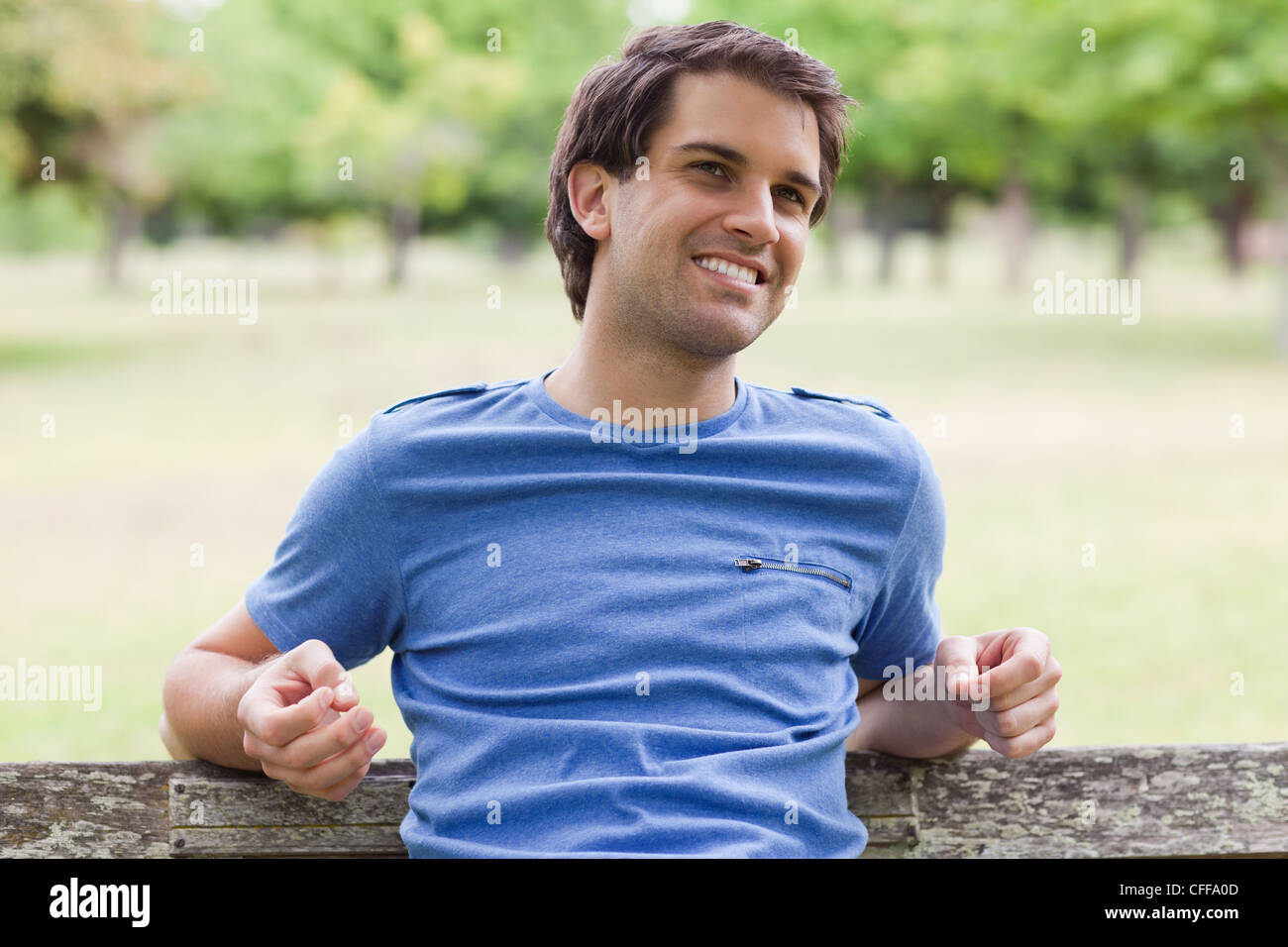 Young smiling man sitting on a bench Stock Photo - Alamy
